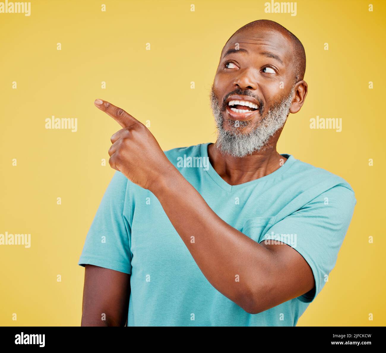 Mature african man smiling and pointing in a direction against a yellow ...