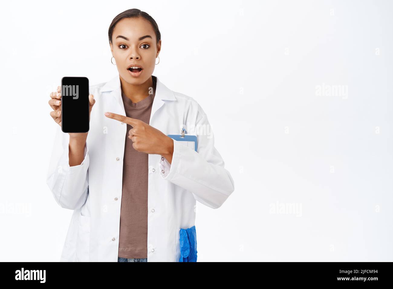 Surprised female doctor, pointing at smartphone app screen, standing ...