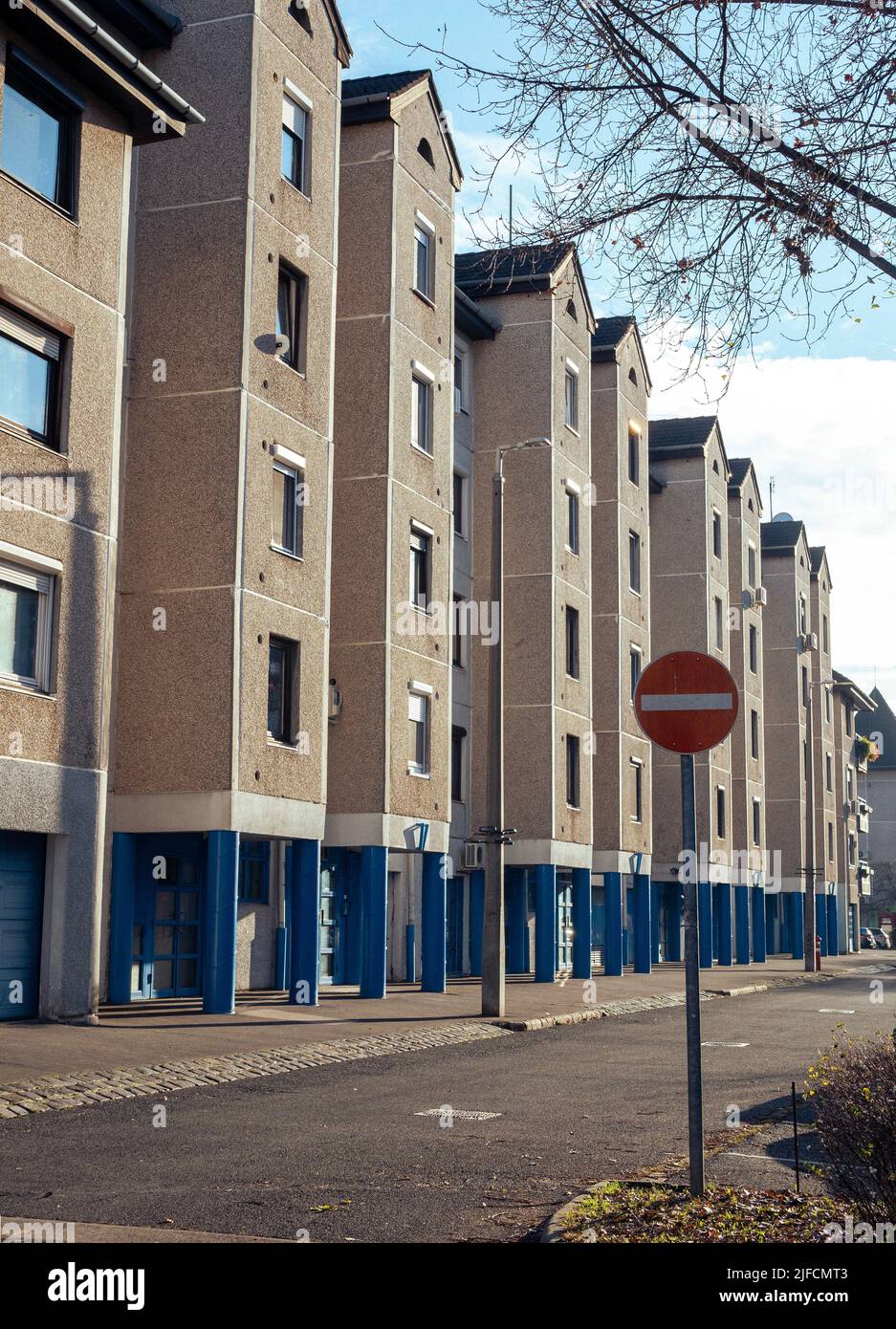 A street with buildings painted blue at the bottom and a red road sign ...