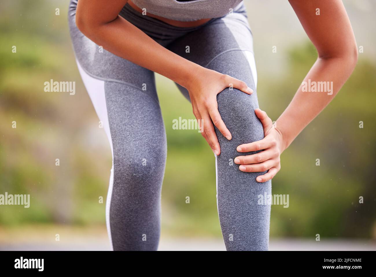 Active woman holding her leg in pain while exercising outdoors. Closeup ...