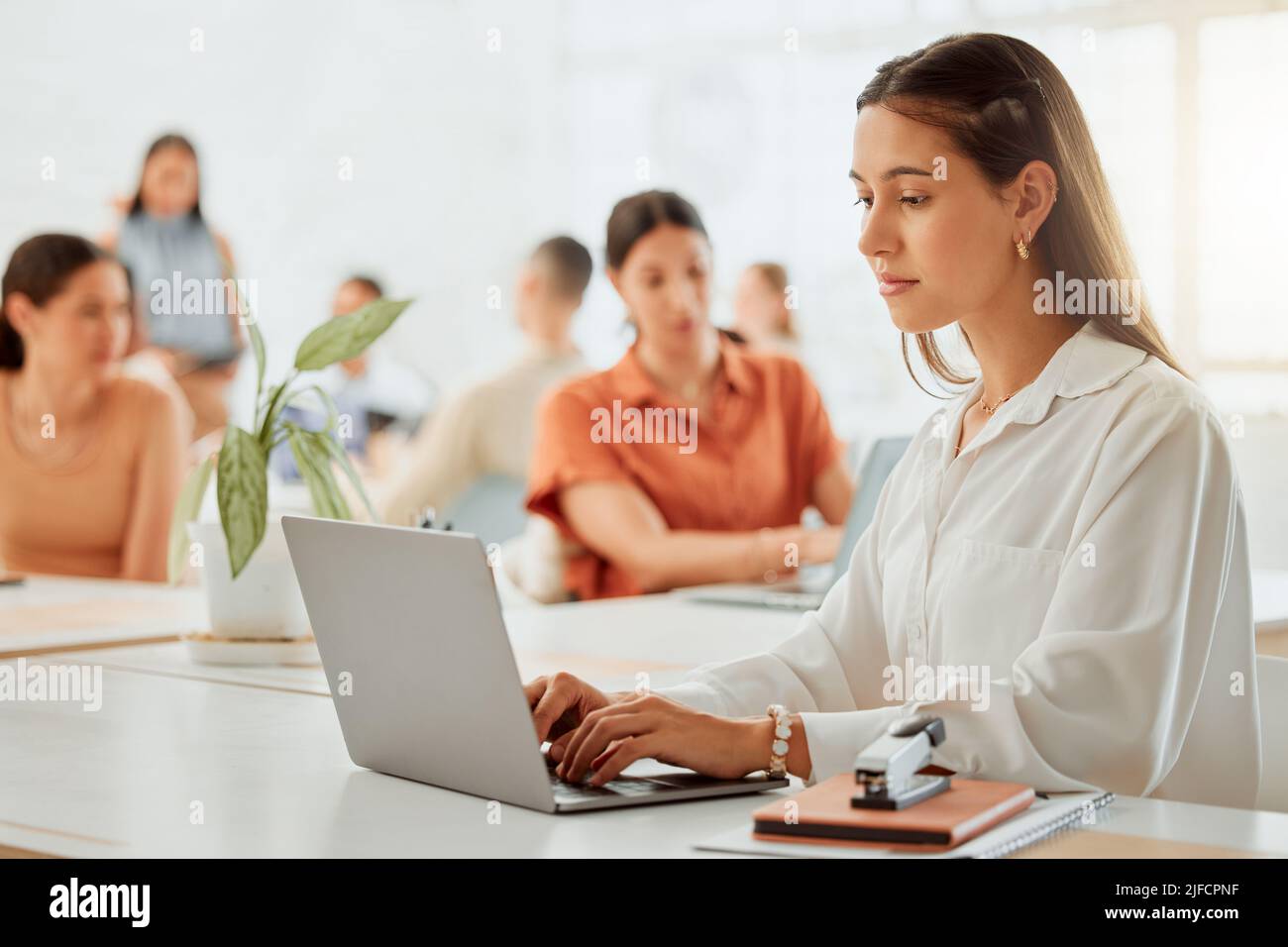 One young hispanic business woman working on a laptop in a busy office ...