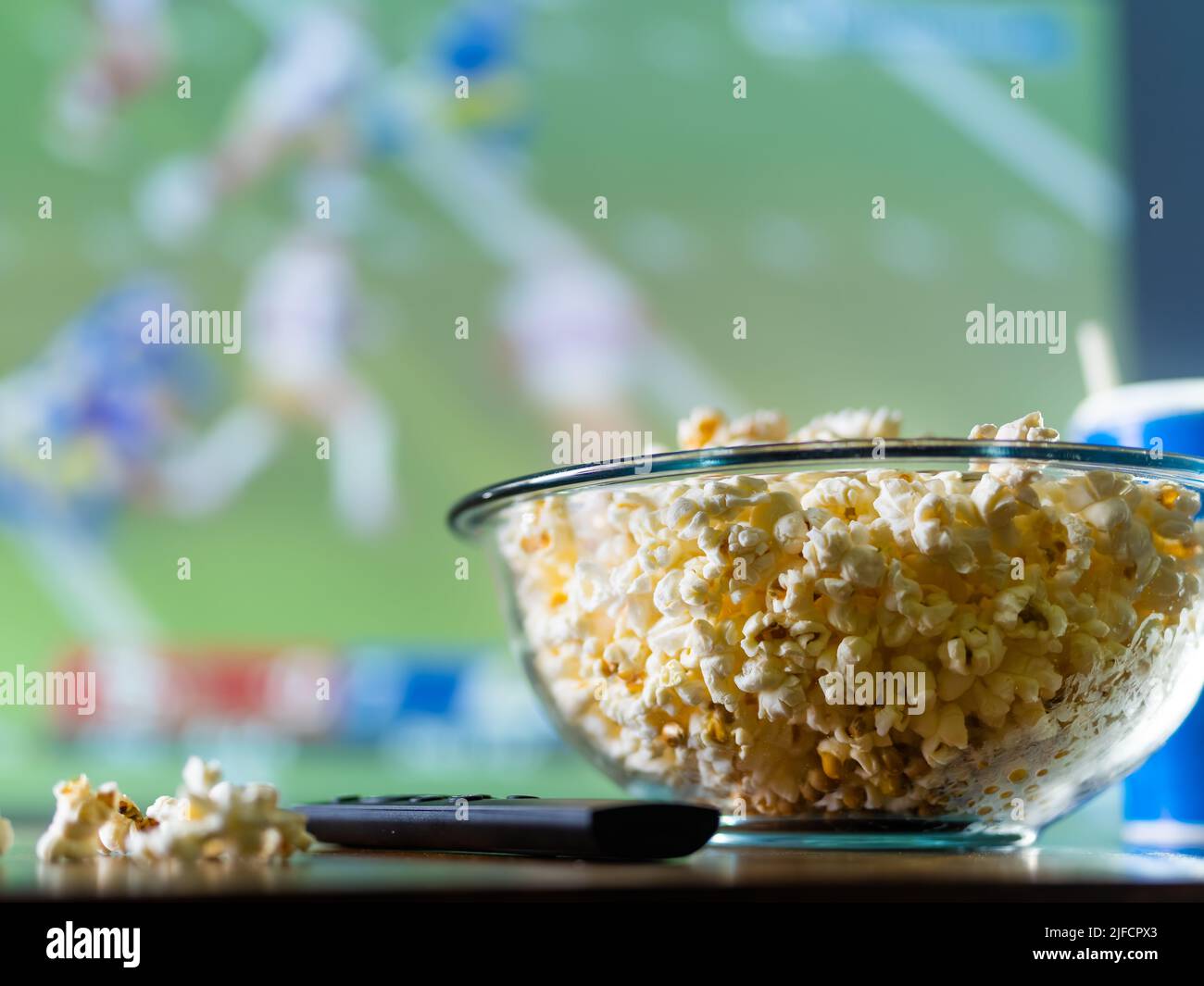 A sports program on the TV screen, a large bowl of popcorn and a TV ...