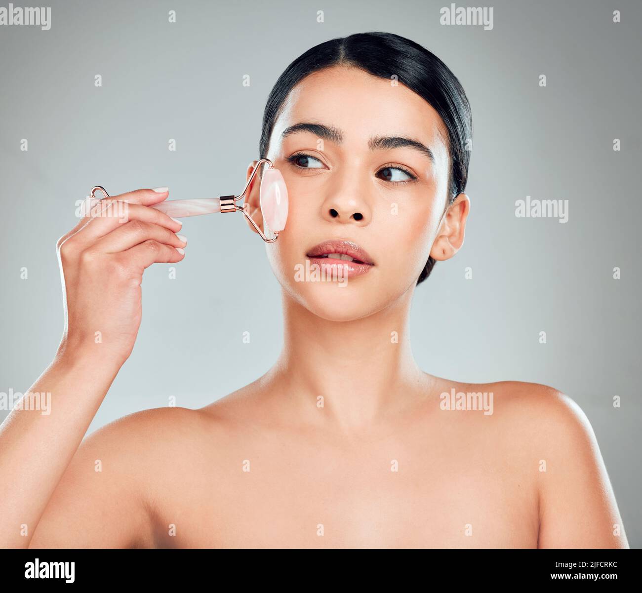 One beautiful mixed race woman using a rose quartz derma roller during ...