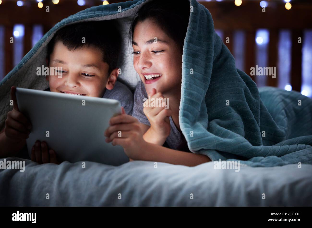 Two kids holding digital tablet while lying under blanket in the dark ...