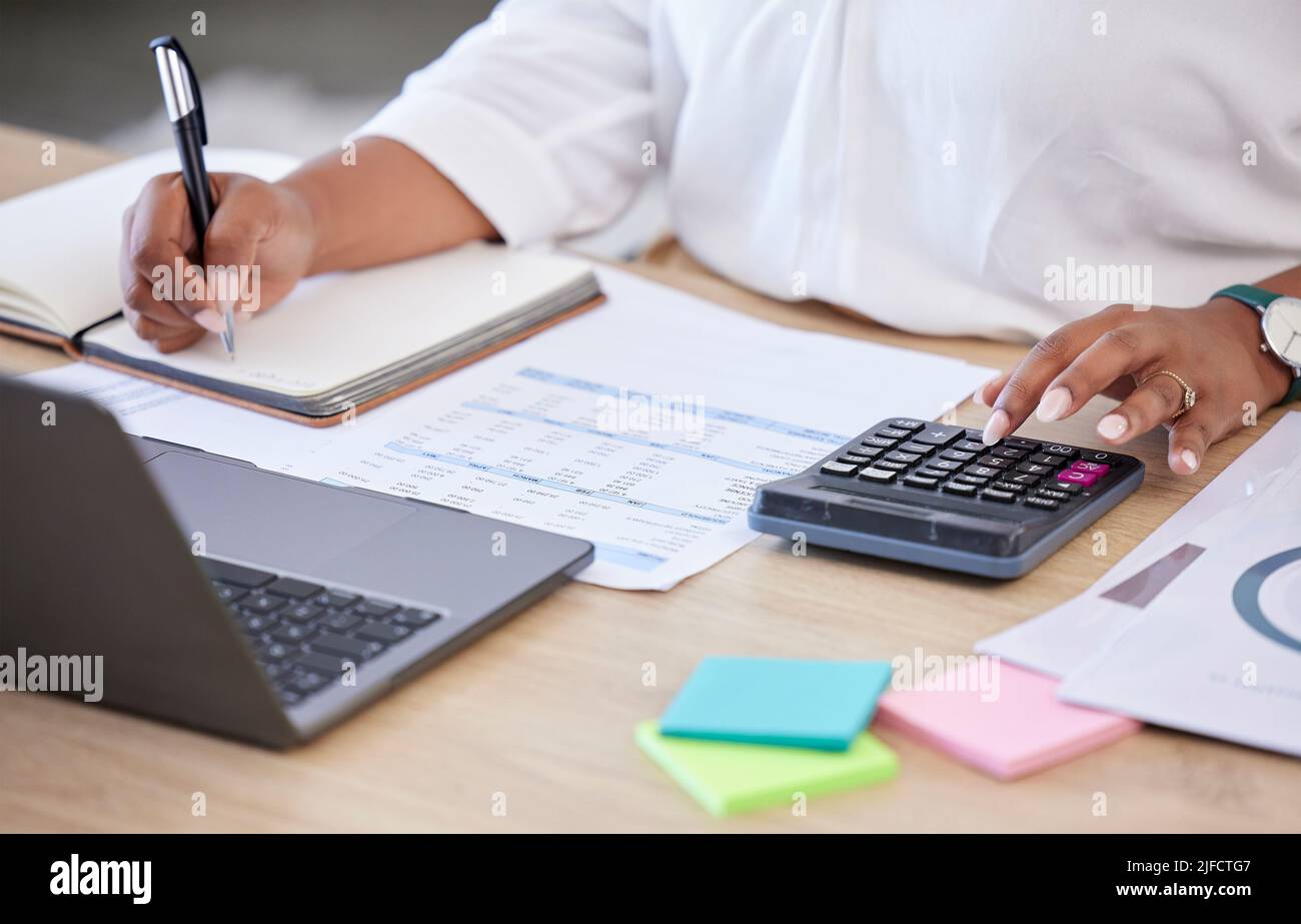 Businessperson using a calculator while writing in a notebook working ...