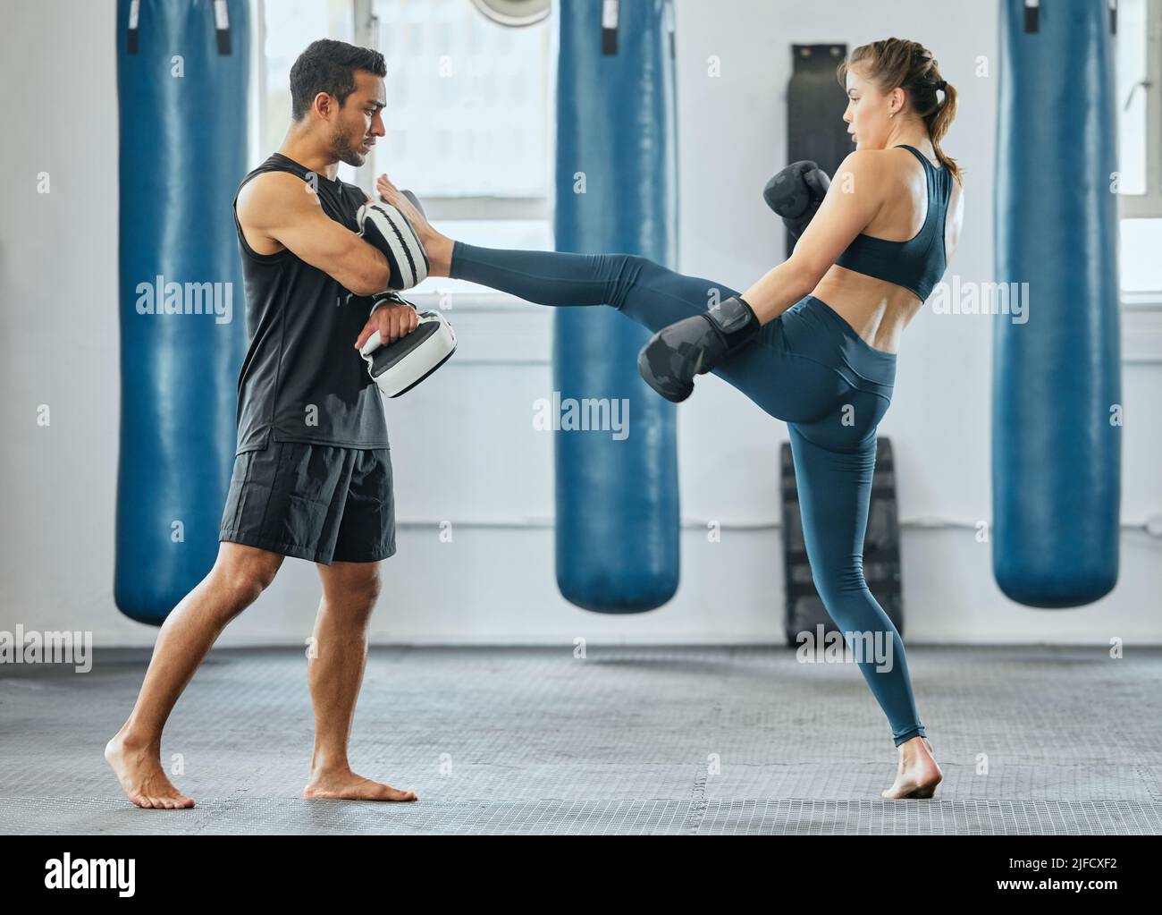 . Female kickboxer at gym with her trainer. Man wearing boxing pads ...
