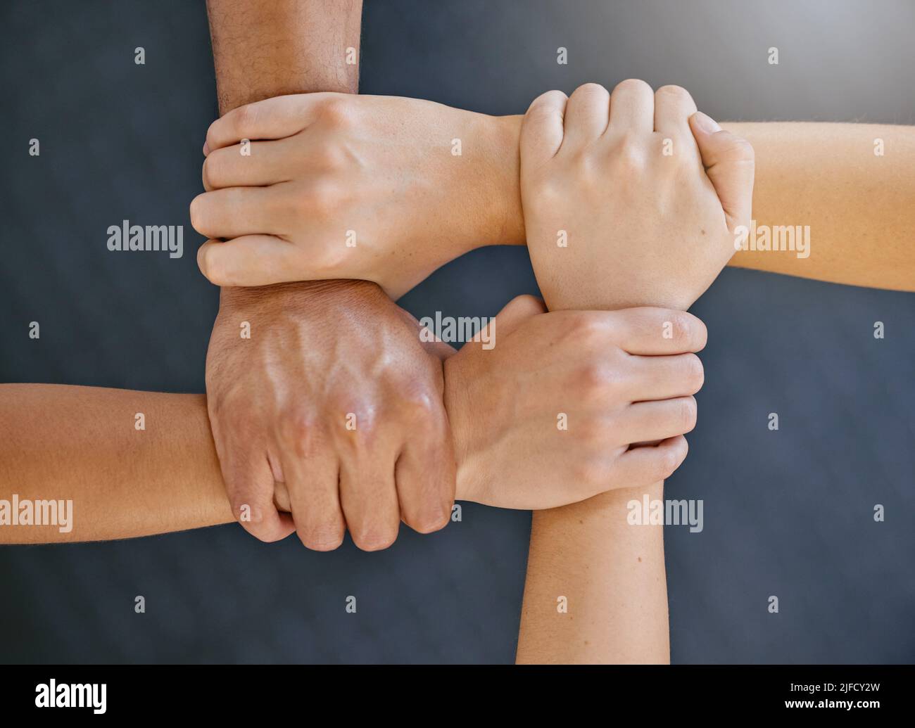 Closeup of diverse group of people from above holding each others wrists in a circle to express ...