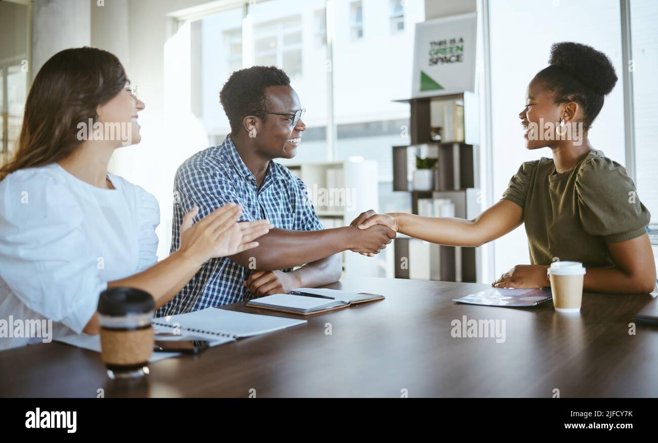 Young happy businesspeople shaking hands in a meeting with a colleague ...