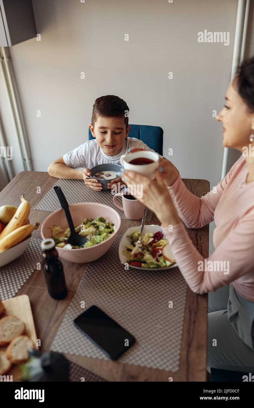 Pretty Caucasian mother and little son doing cheers gesture with cups ...