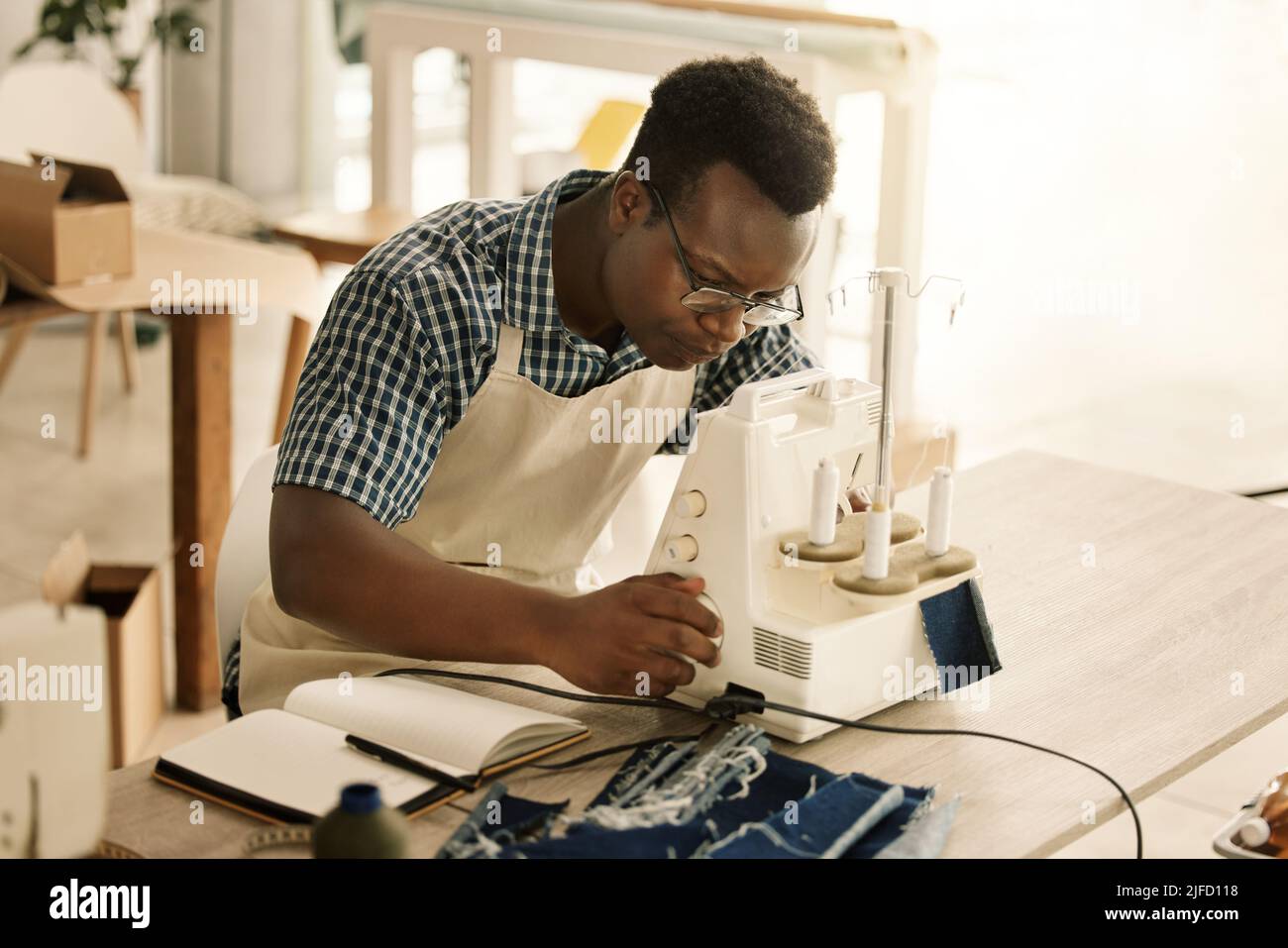 african american tailor sewing a piece of denim. Young designer using ...