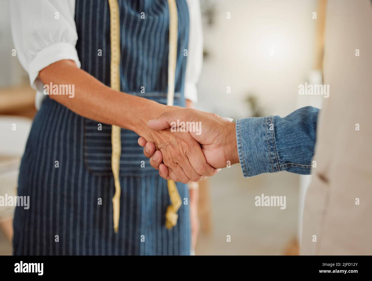 Two clothing designers shaking hands while working together at a shop ...
