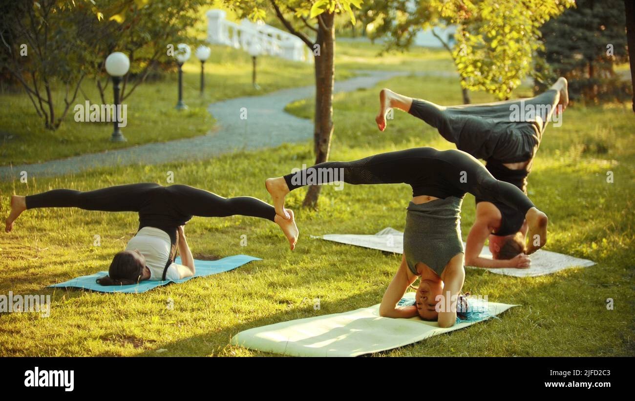 Two young women doing yoga exercises with a trainer in the park near ...