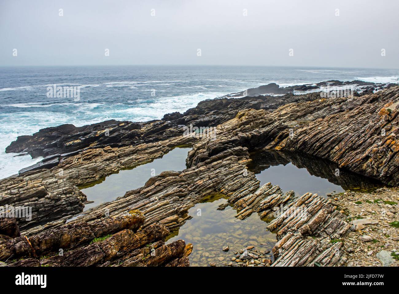 Sheltered tidal pools along the jagged and tilted rock strata of the ...