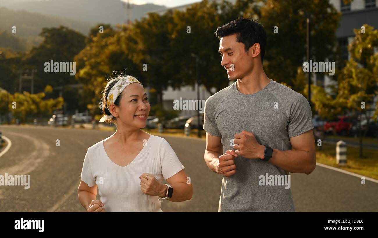Shot of active middle aged woman jogging with personal trainer at the ...