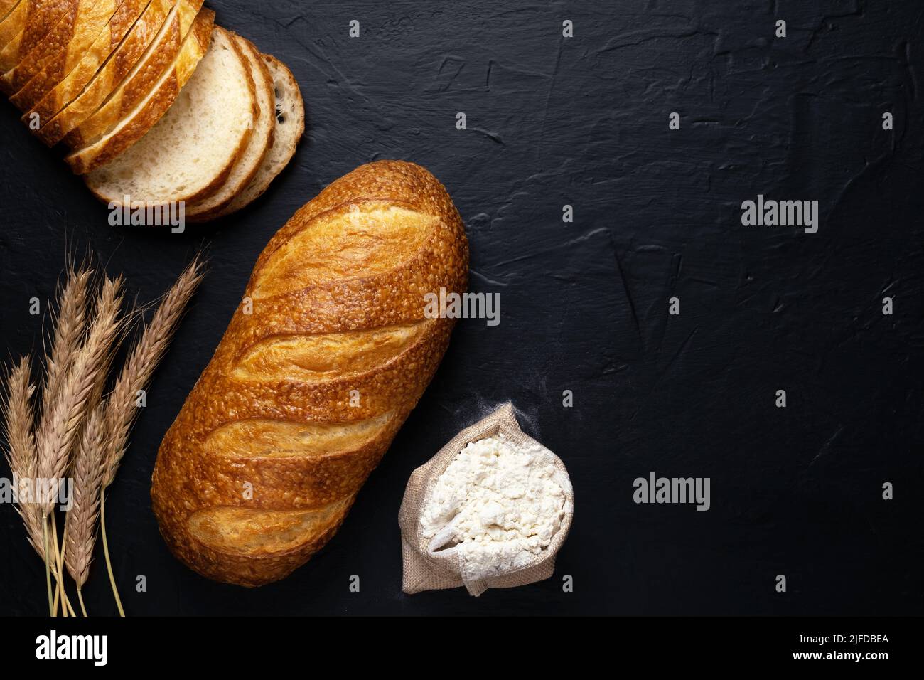 Fresh wheaten baton bread and flour on dark background.Top view. Copy ...
