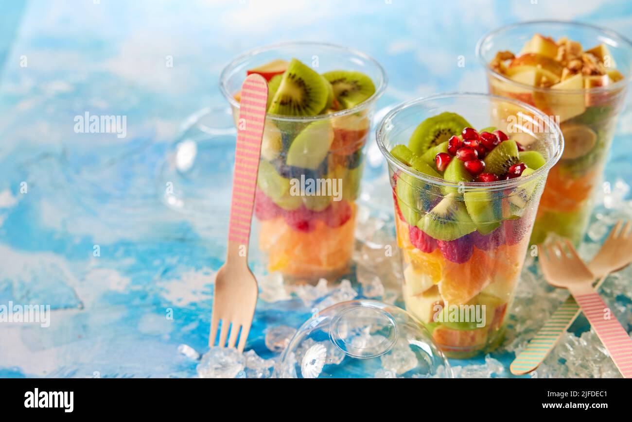 Mix of fresh tasty chopped fruits in plastic cups to go placed on table ...