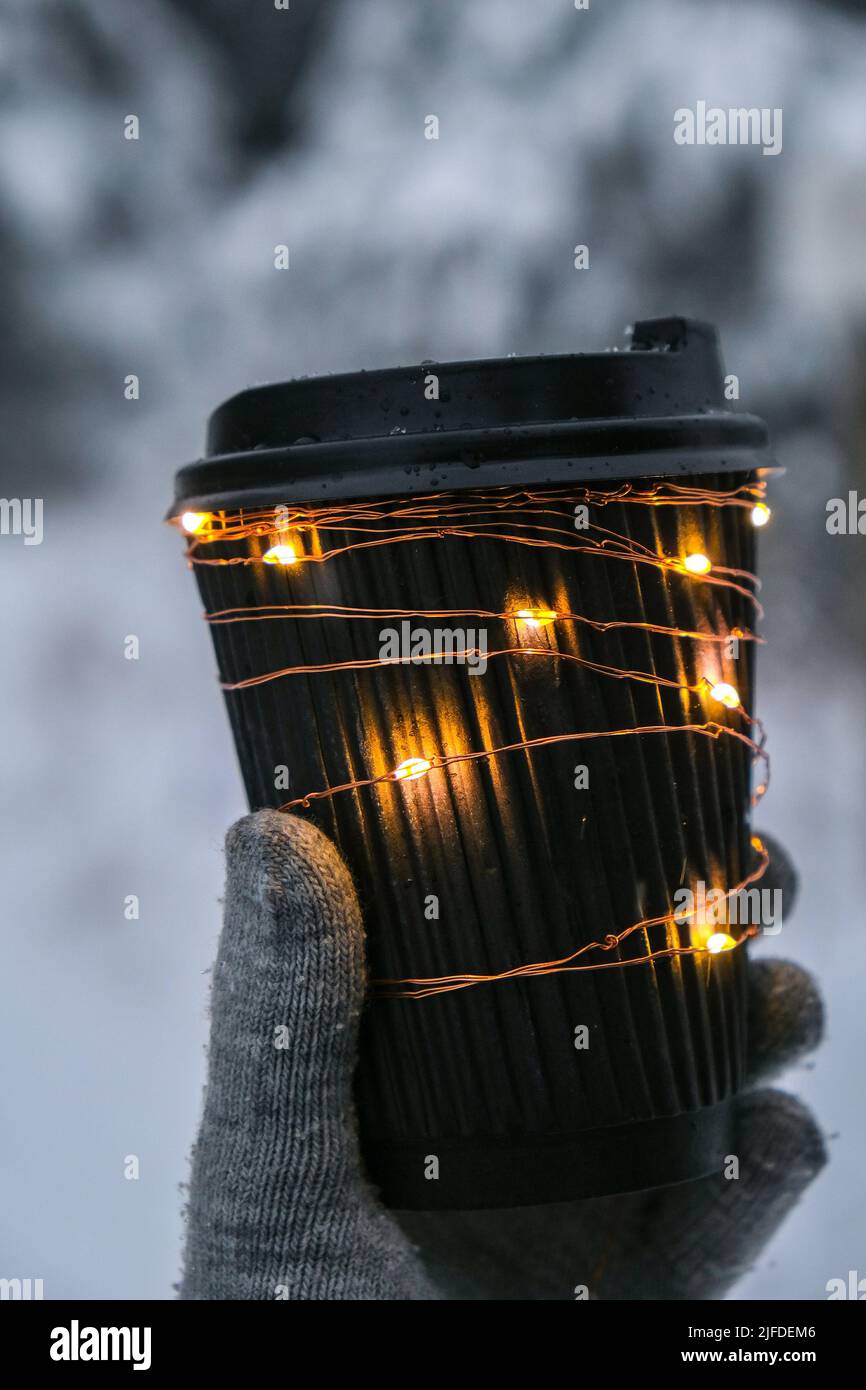 Female hand in winter warm gloves holding black eco paper cup with ...