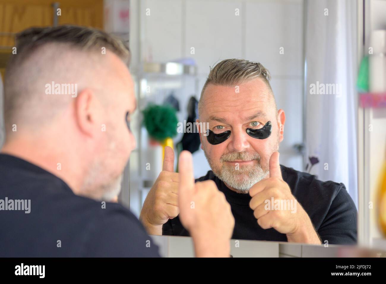 Senior man pointing to hydrating gel eye patches while giving a thumbs ...