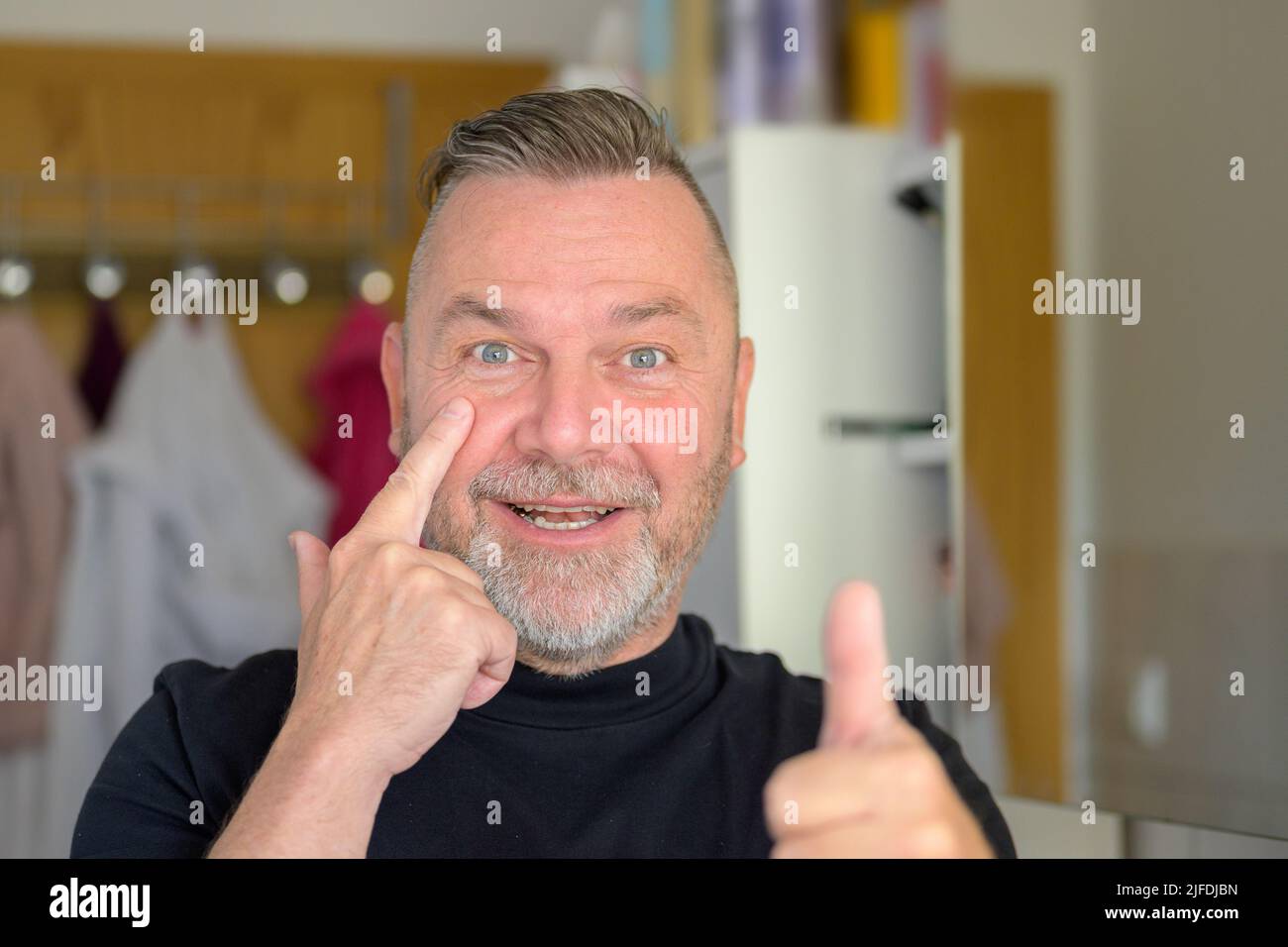 Satisfied man giving a thumbs up and pointing to his eyes after using ...