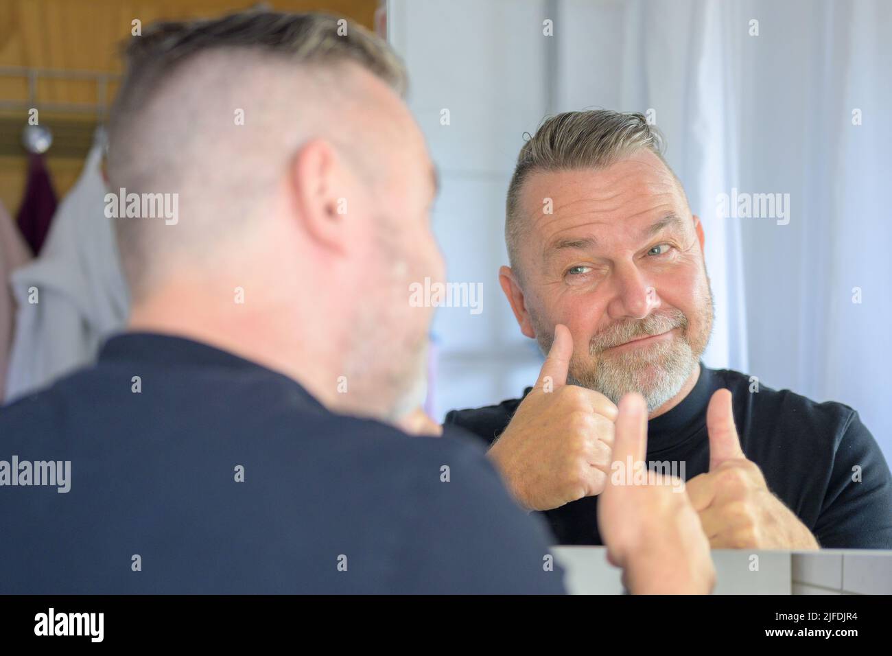 Smiling satisfied man looking at himself in the mirror and giving a ...