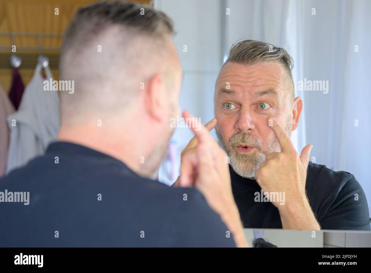 Man examining his face in a mirror after applying hydration patches ...