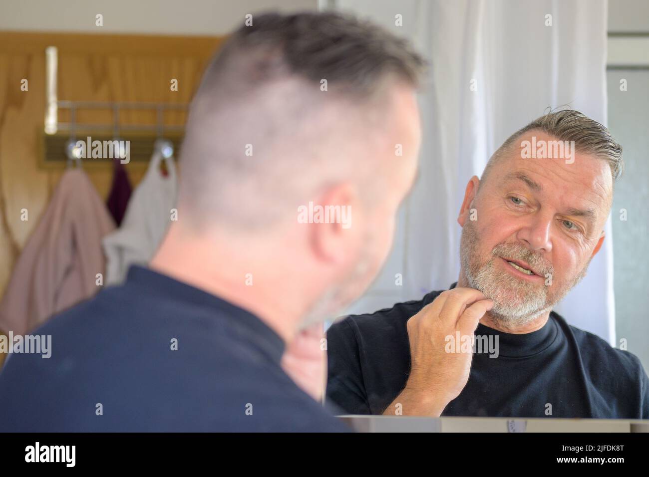 Man checking out his neatly trimmed beard in the mirror running his ...