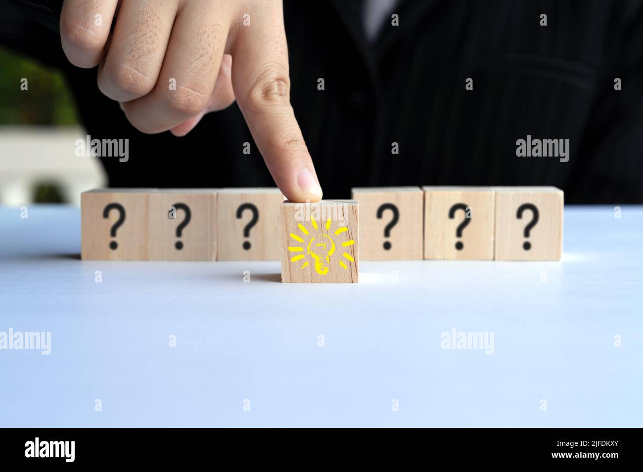 Hand Pointing at wooden cube block with light bulb with questions marks ...