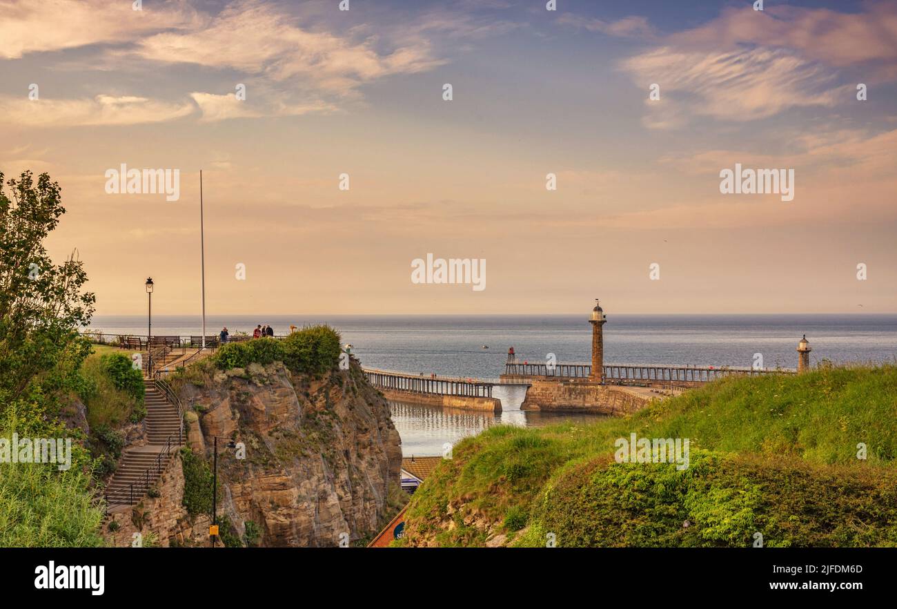 A pier and a lighthouse seen through a gap between two cliffs. An ...