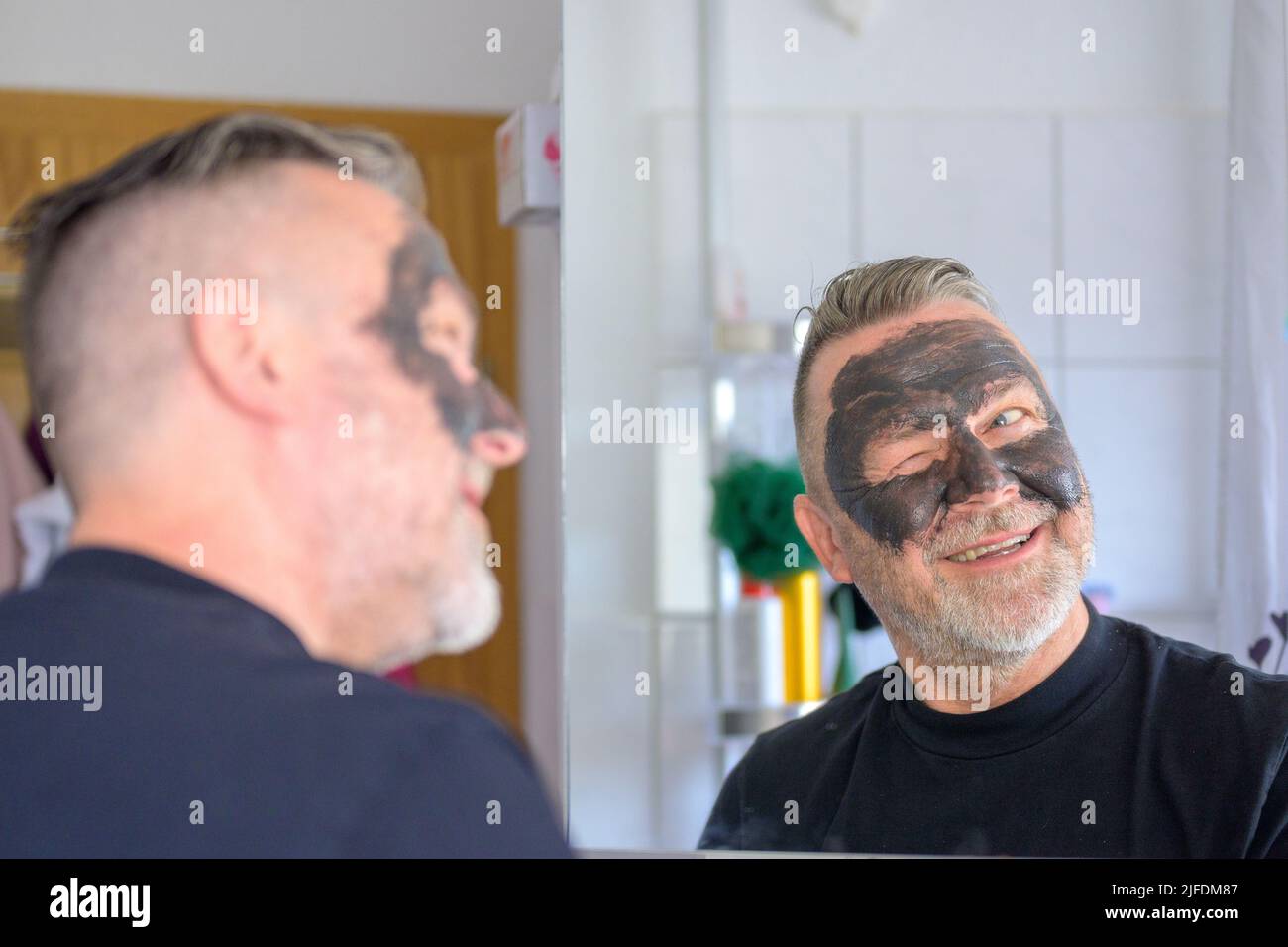 Happy healthy egotistical man using a face mask to care for his skin ...
