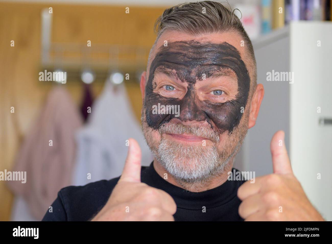 Jubilant senior man doing a skin care treatment using a face mask ...