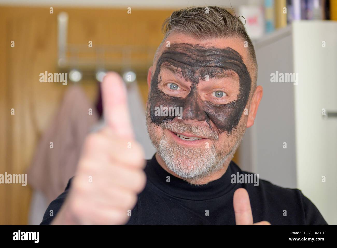 Happy healthy man using facial skin care products wearing a face mask ...