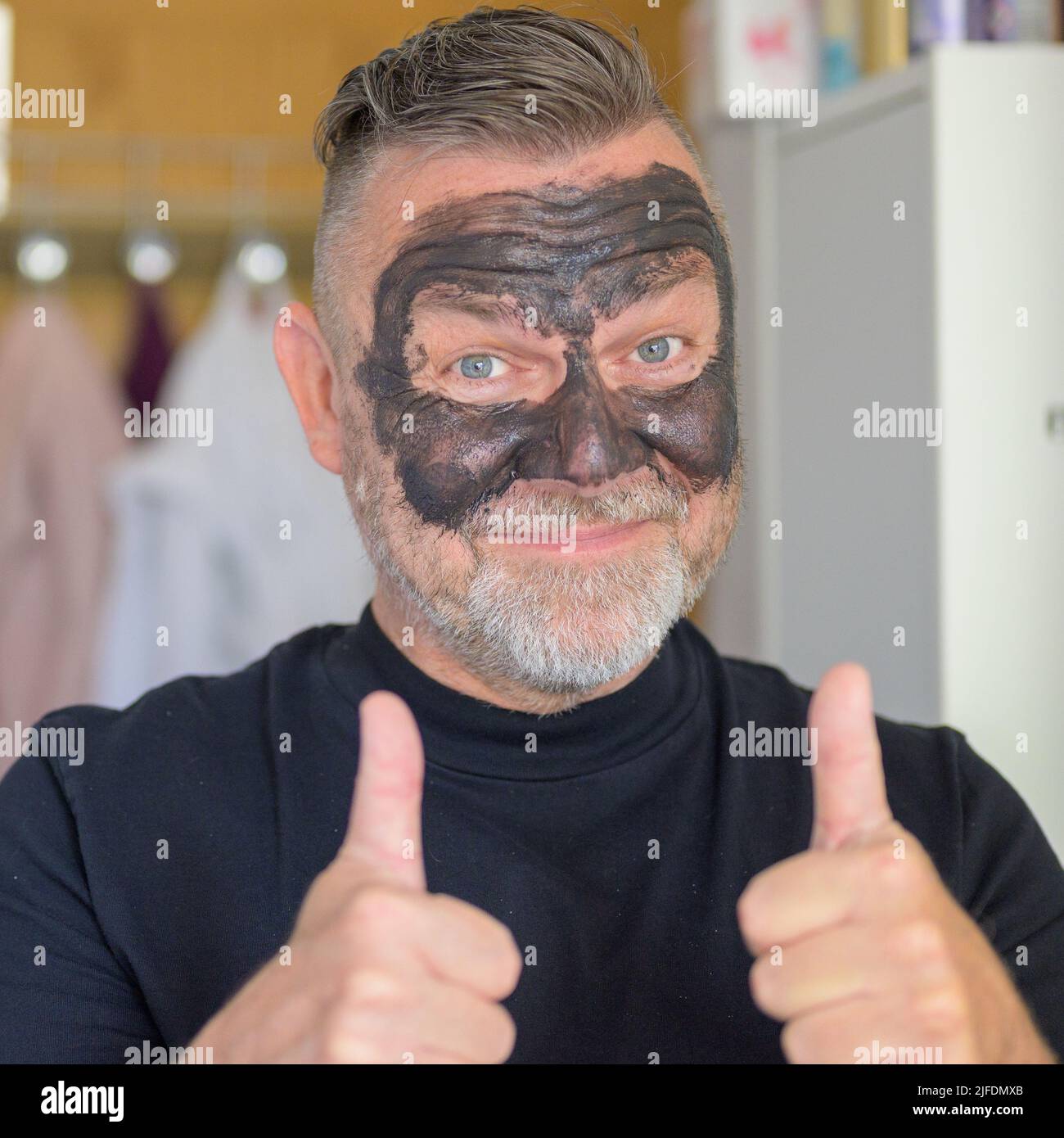 Happy healthy man using facial skin care products wearing a face mask ...