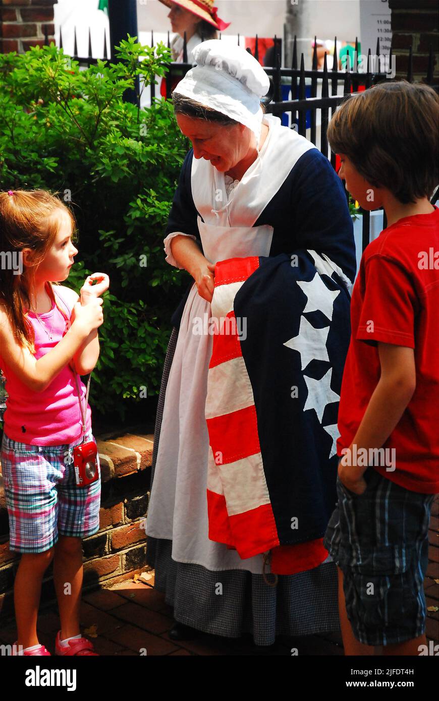 A Betsy Ross Reenactor demonstrates early flag making to two children ...