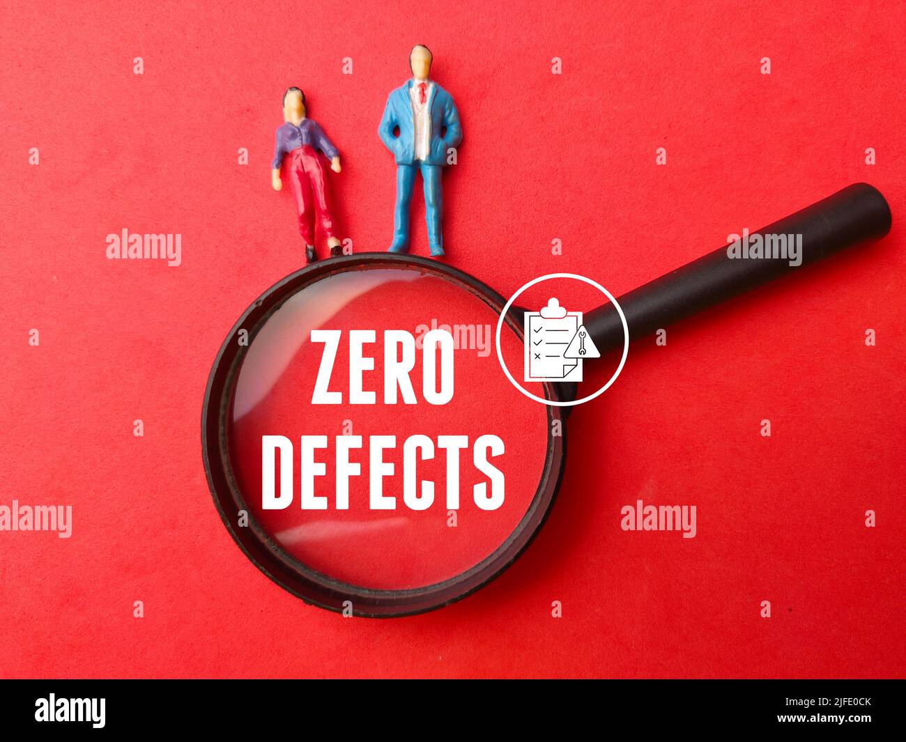 A shot of miniature people and an icon with text ZERO DEFECTS on a red ...