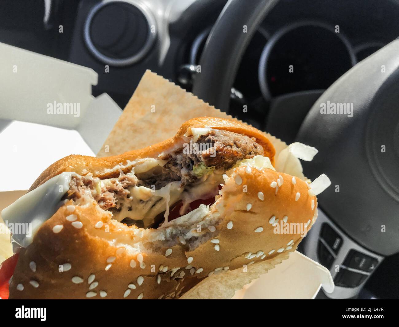 Eating while driving: a bitten burger in the hands inside the car ...