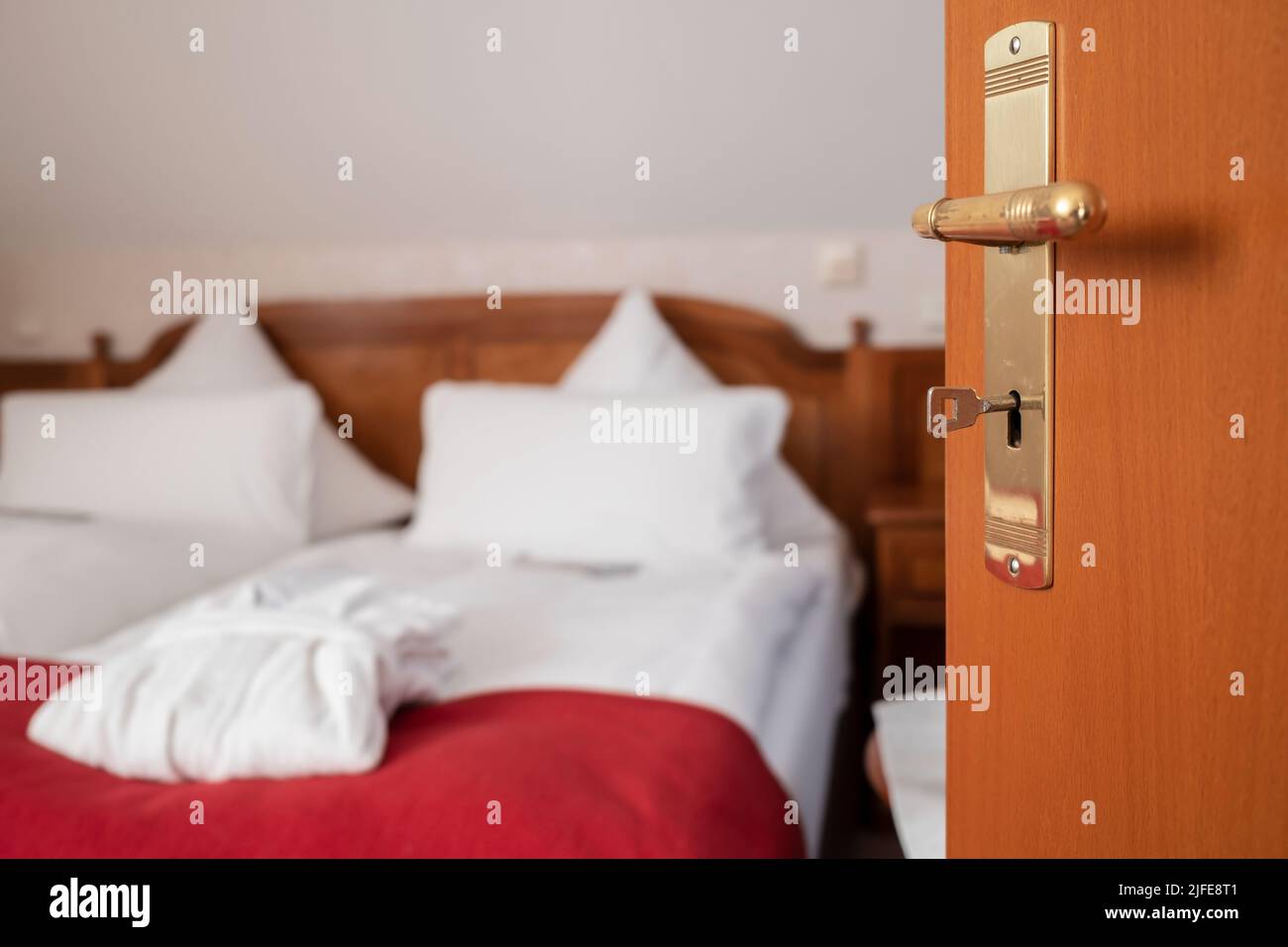 Ajar wooden door with a key to a hotel room, through which a bedroom is ...