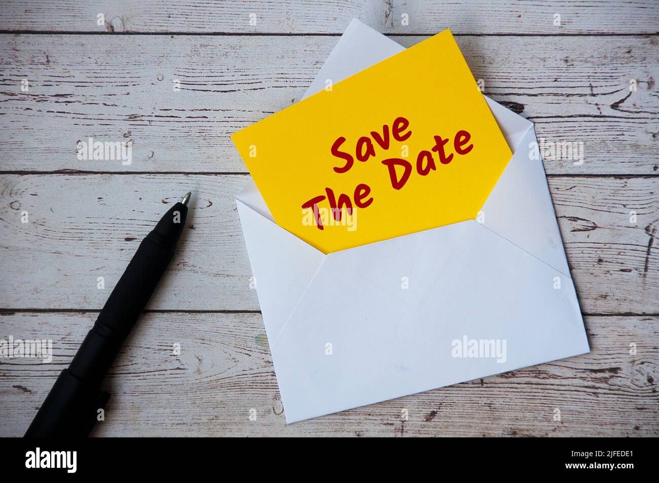 Save the date text on yellow notepad in an envelope with pen and wooden ...