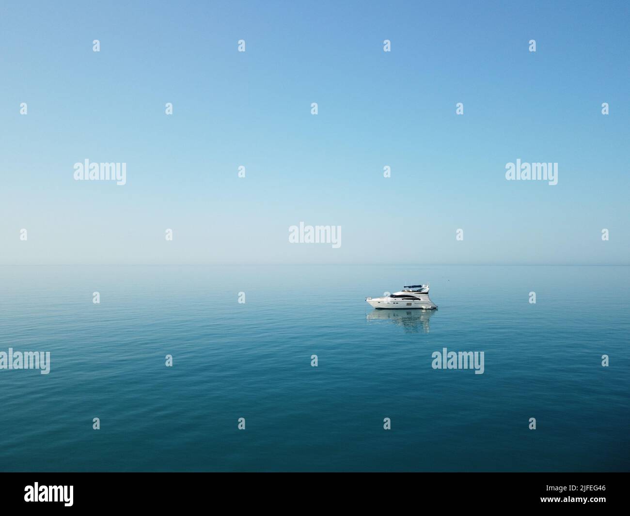 Aerial yacht on calm sea. Luxury cruise trip. View from above of white boat on deep blue water ...