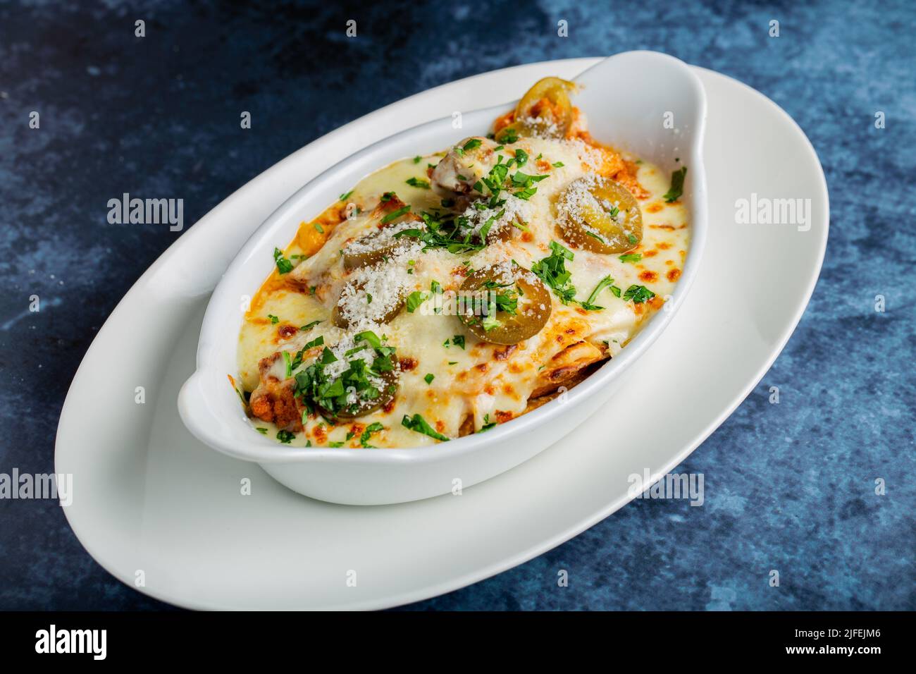 A freshly baked lasagna with lots of cheese toppings on a white plate ...