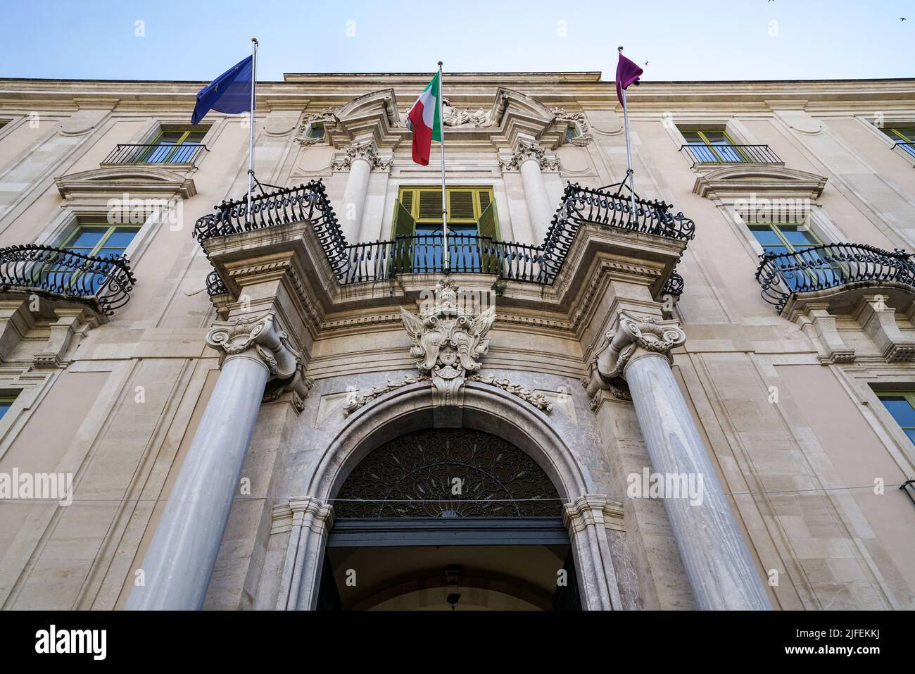 A low angle shot of the University of Catania's facade with three flags ...