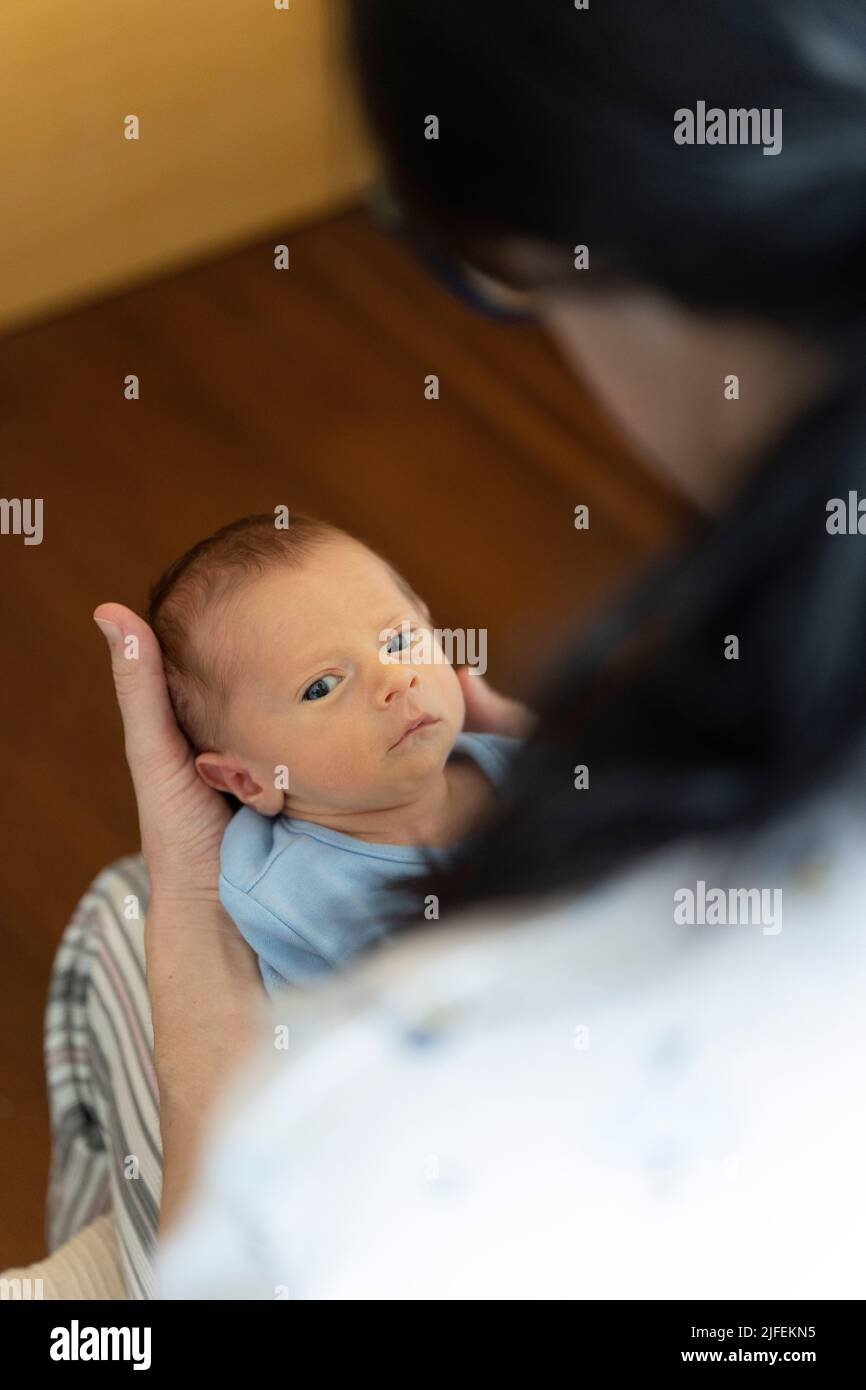 Small newborn baby looking at camera while being held by young woman ...