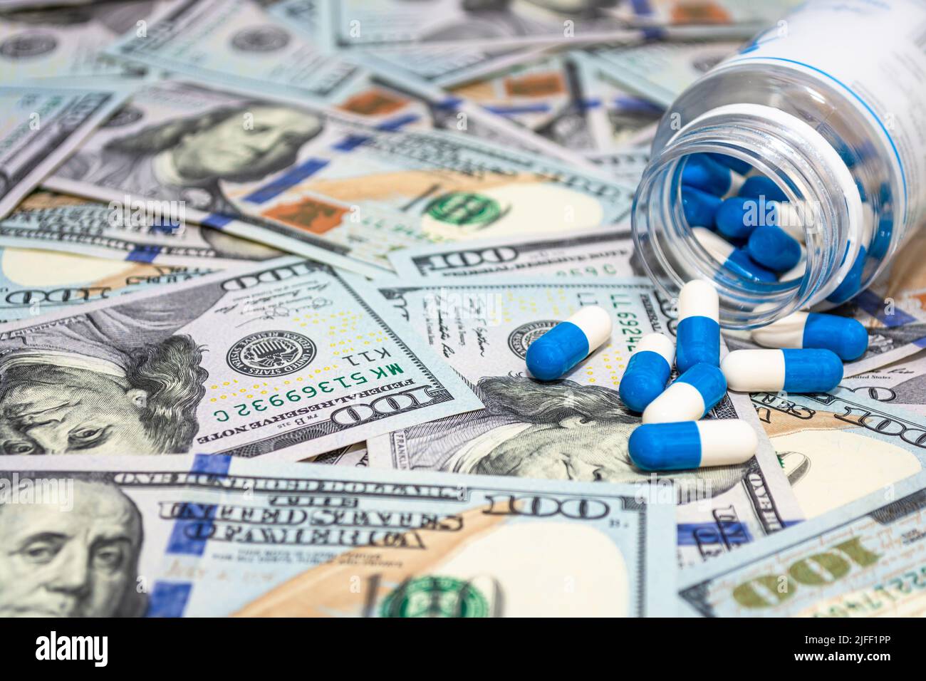 Money and drugs, pharmaceuticals. Blue-white pills are scattered from a ...