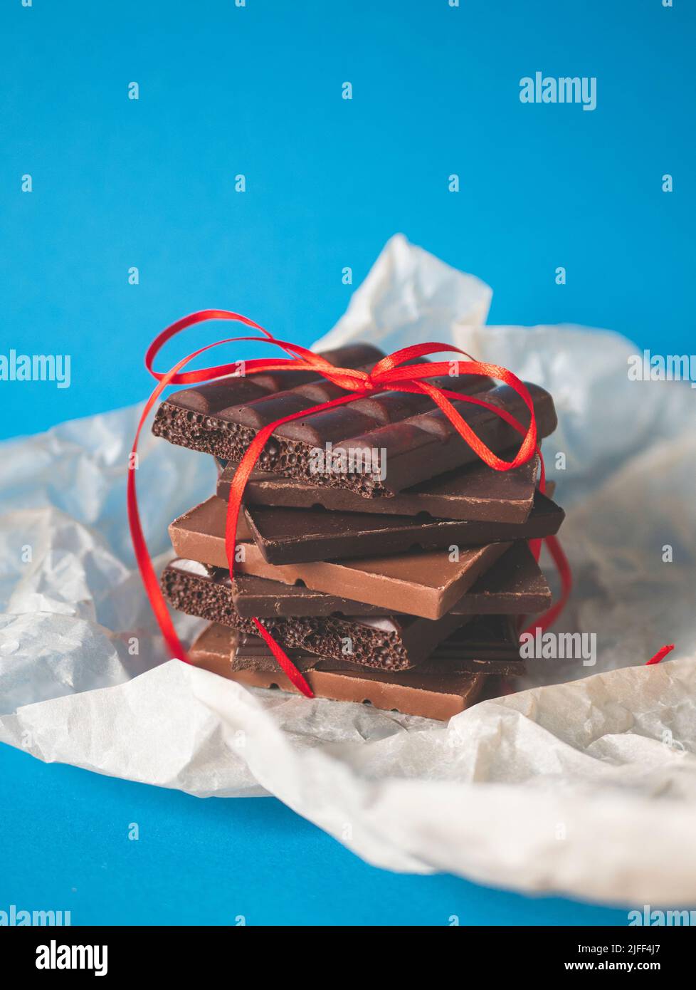 Stack of assorted chocolate pieces tied with a red ribbon on blue ...