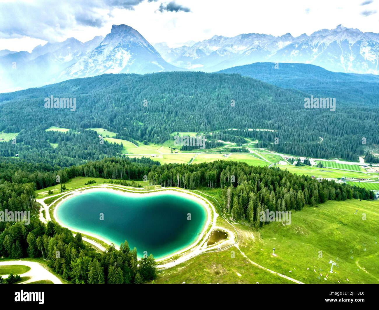 An aerial view of a small lake surrounded by trees with mountains and ...