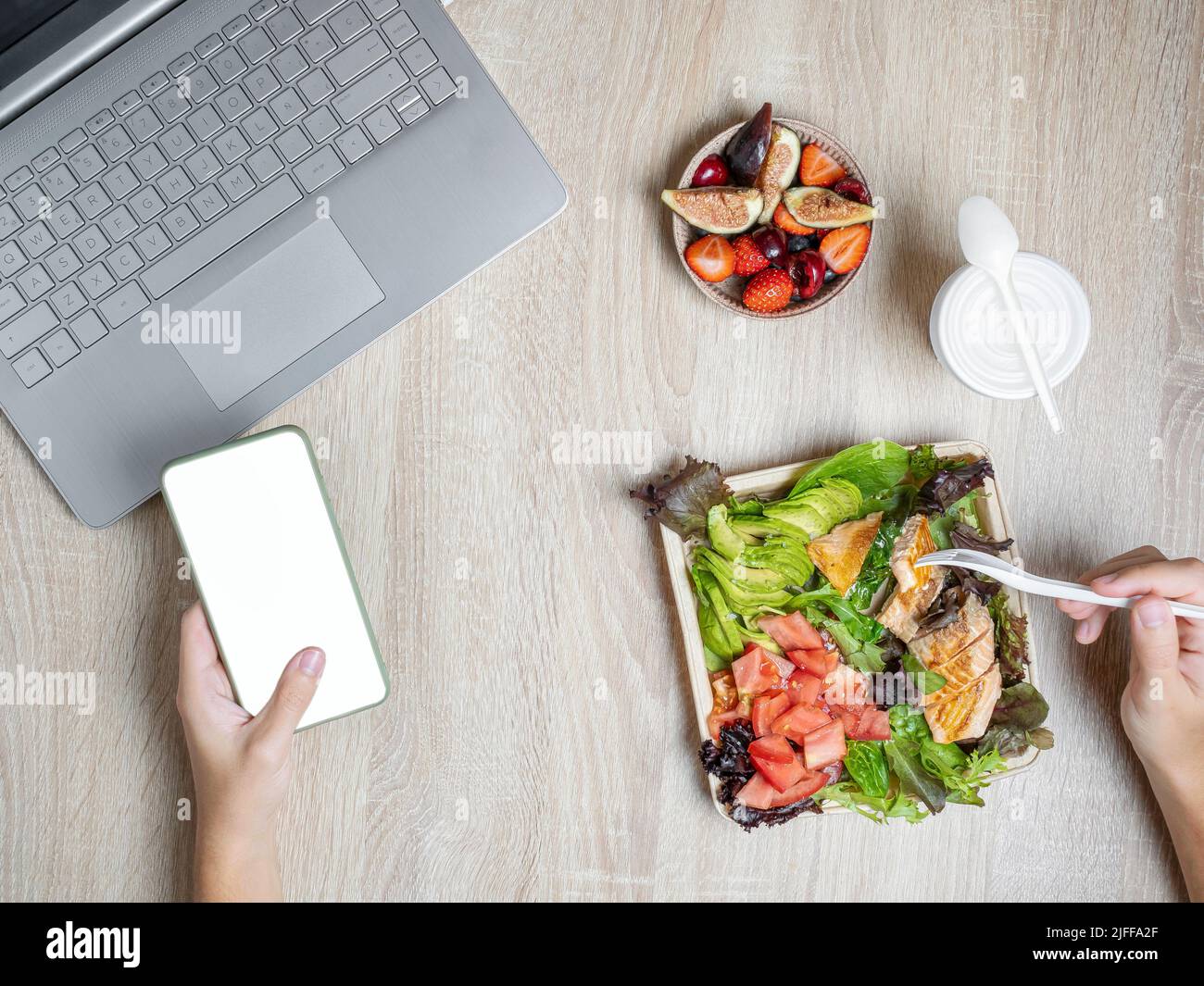 Workspace with laptop, one hand holding a cell phone and the other with ...