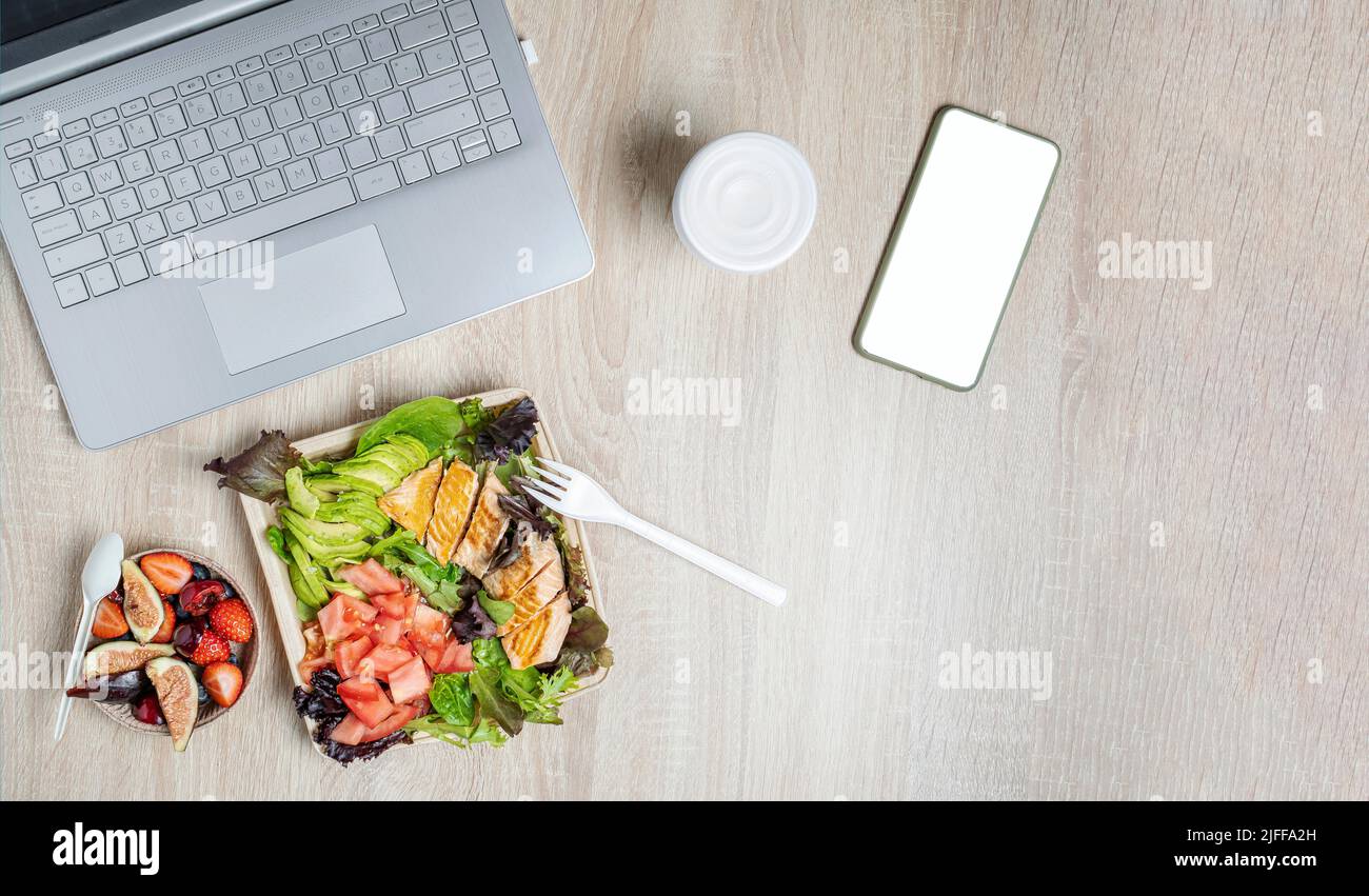 Workspace with laptop, healthy food takeaway, fruit of the forest and ...