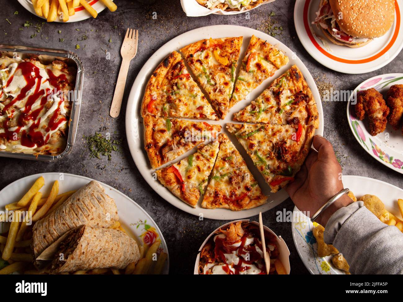 A man's hand picks up a slice of pizza at the table in the fast food ...