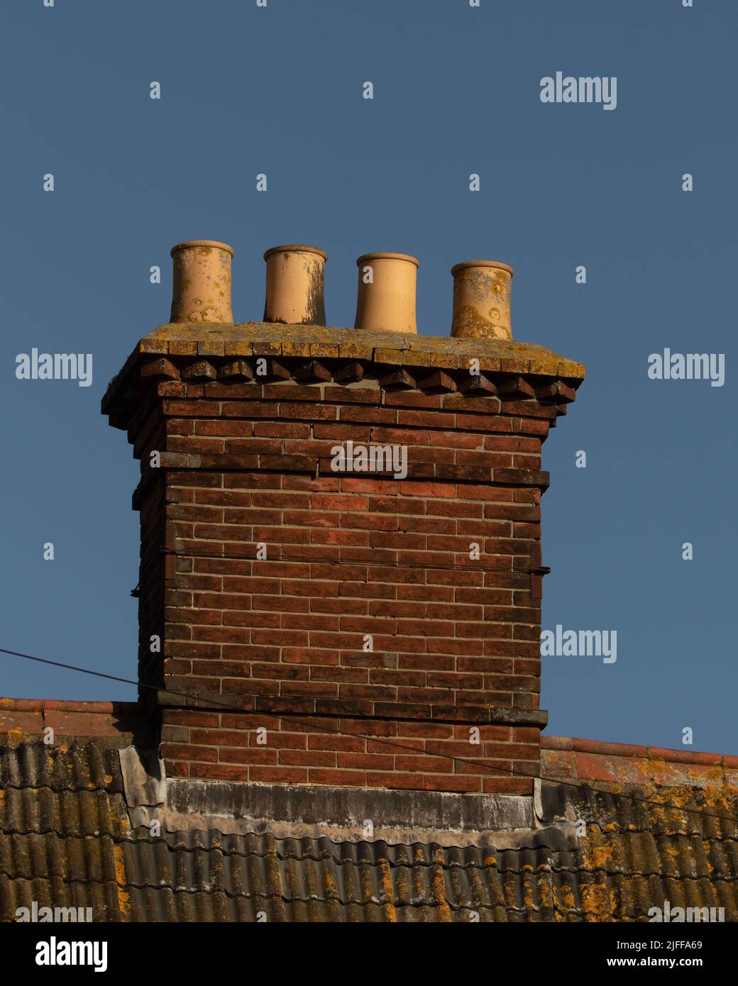A view of four weathered chimney pots on red brick chimney stack and ...