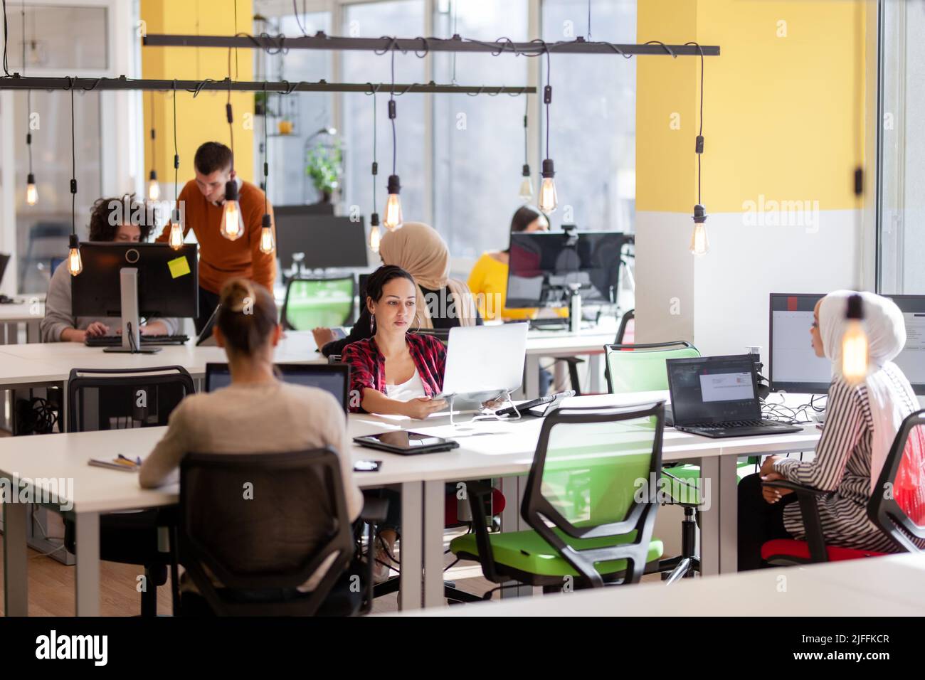 Creative team of young individuals working on desktop computers in a ...