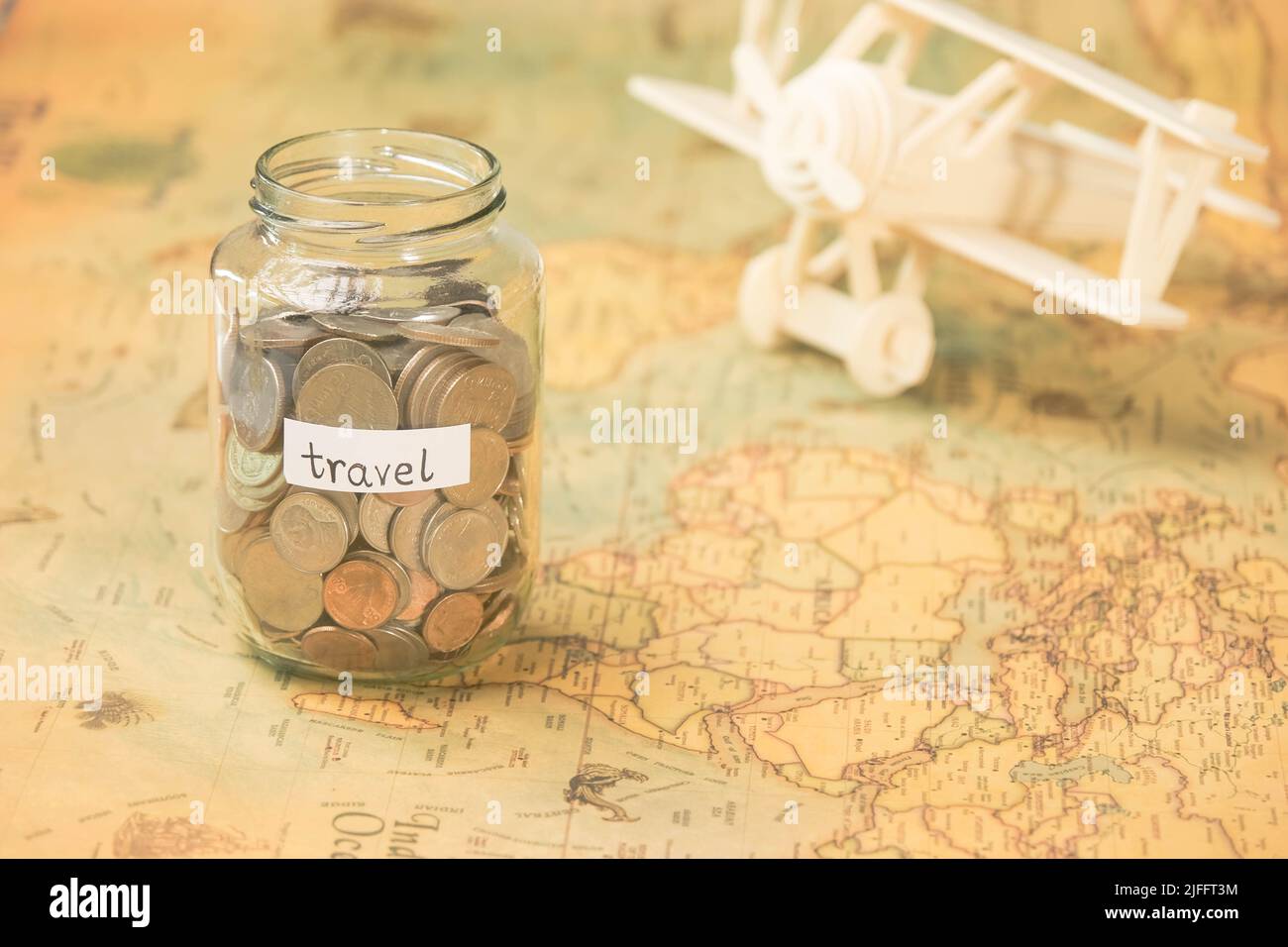 Glass jar with coins and travel inscription on world map with wooden ...
